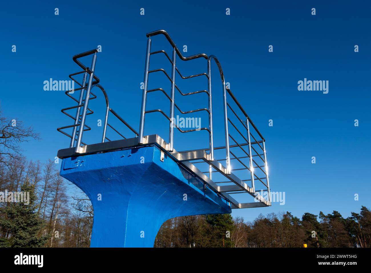 A blue diving board over an empty swimming pool. Stainless steel rails ...