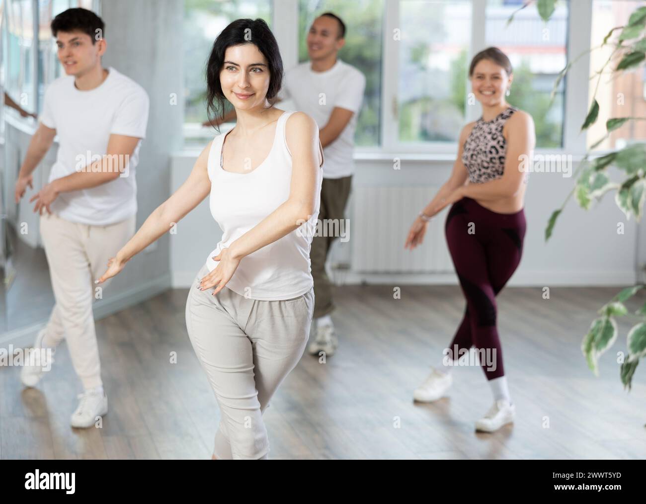Positive young girl dancing vigorous swing with other people during ...