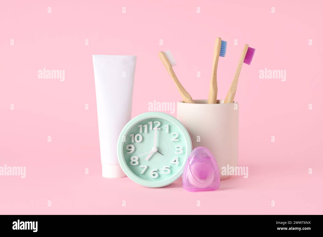Clock, toothpaste, dental floss and toothbrushes on pink background ...
