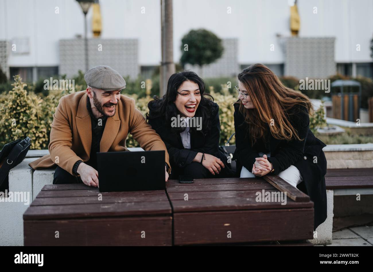 Three friends laughing and sharing fun moments at outdoor seating area ...