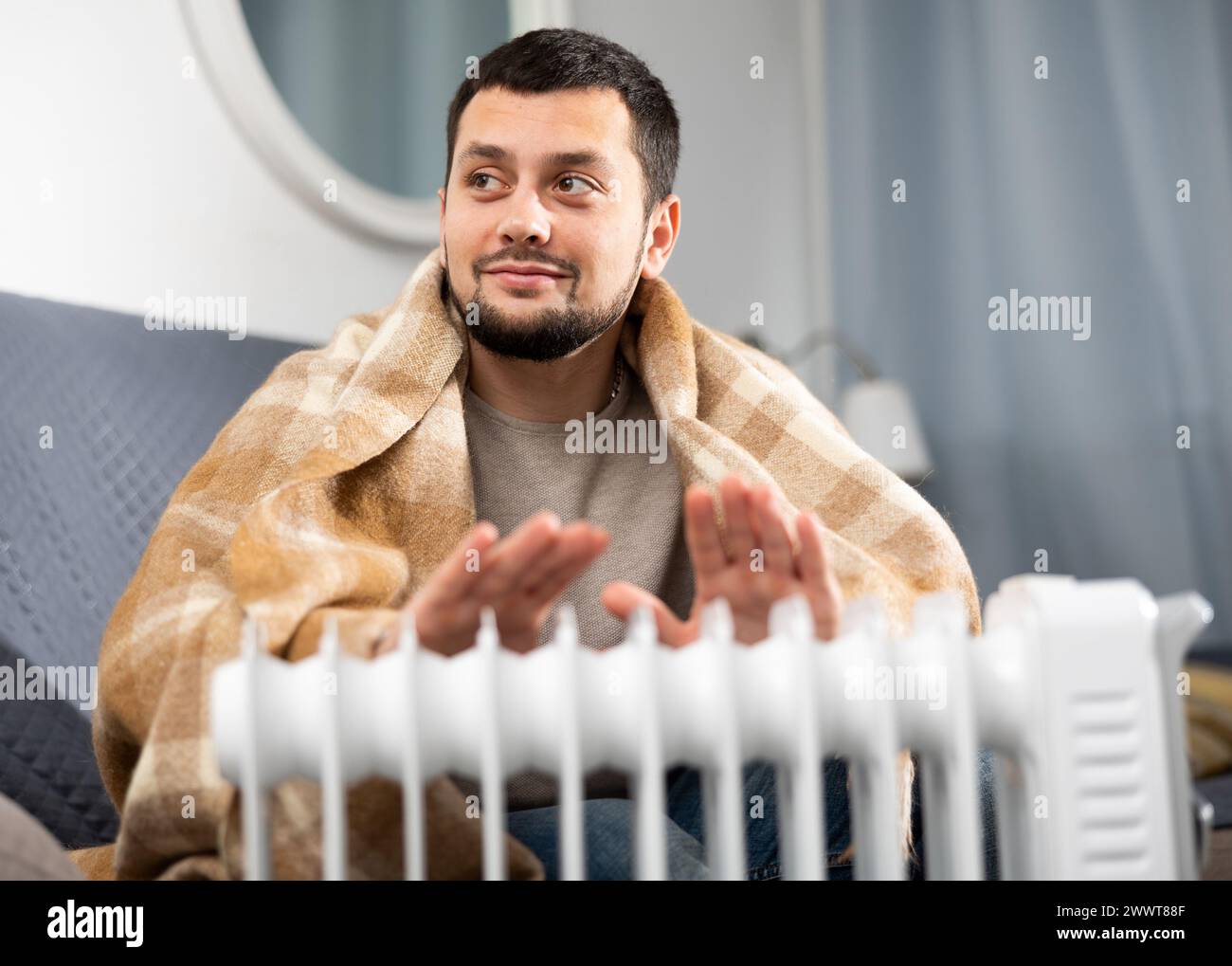 Man wrapped in cover warming hands at radiator in apartment Stock Photo ...