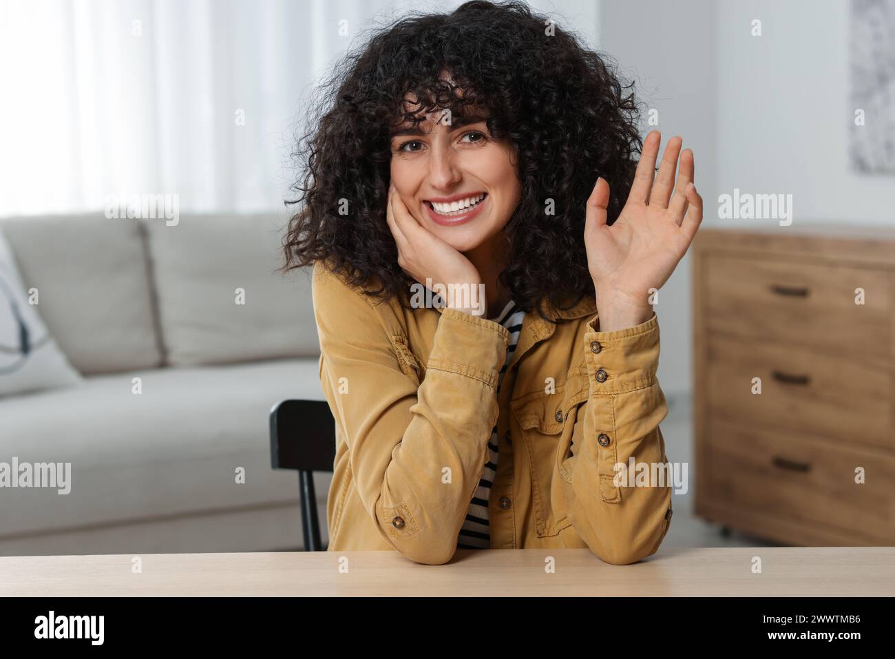 Happy woman waving hello at wooden table in room Stock Photo - Alamy