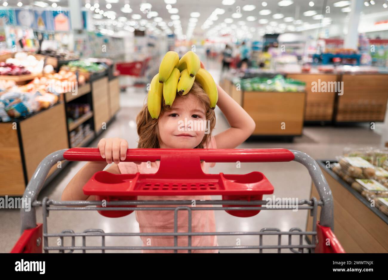 Funny kid with shopping cart buying food at grocery store or ...