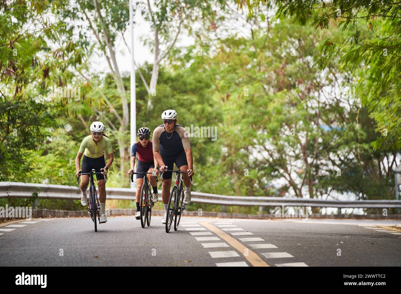 group of three young asian adult cyclists riding bike on rural road ...