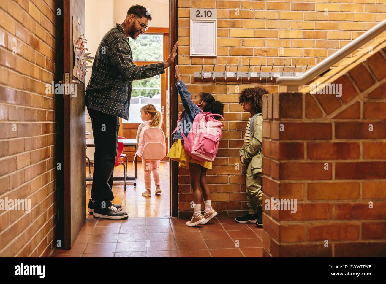 Elementary school teacher greeting his students at the door. Male ...