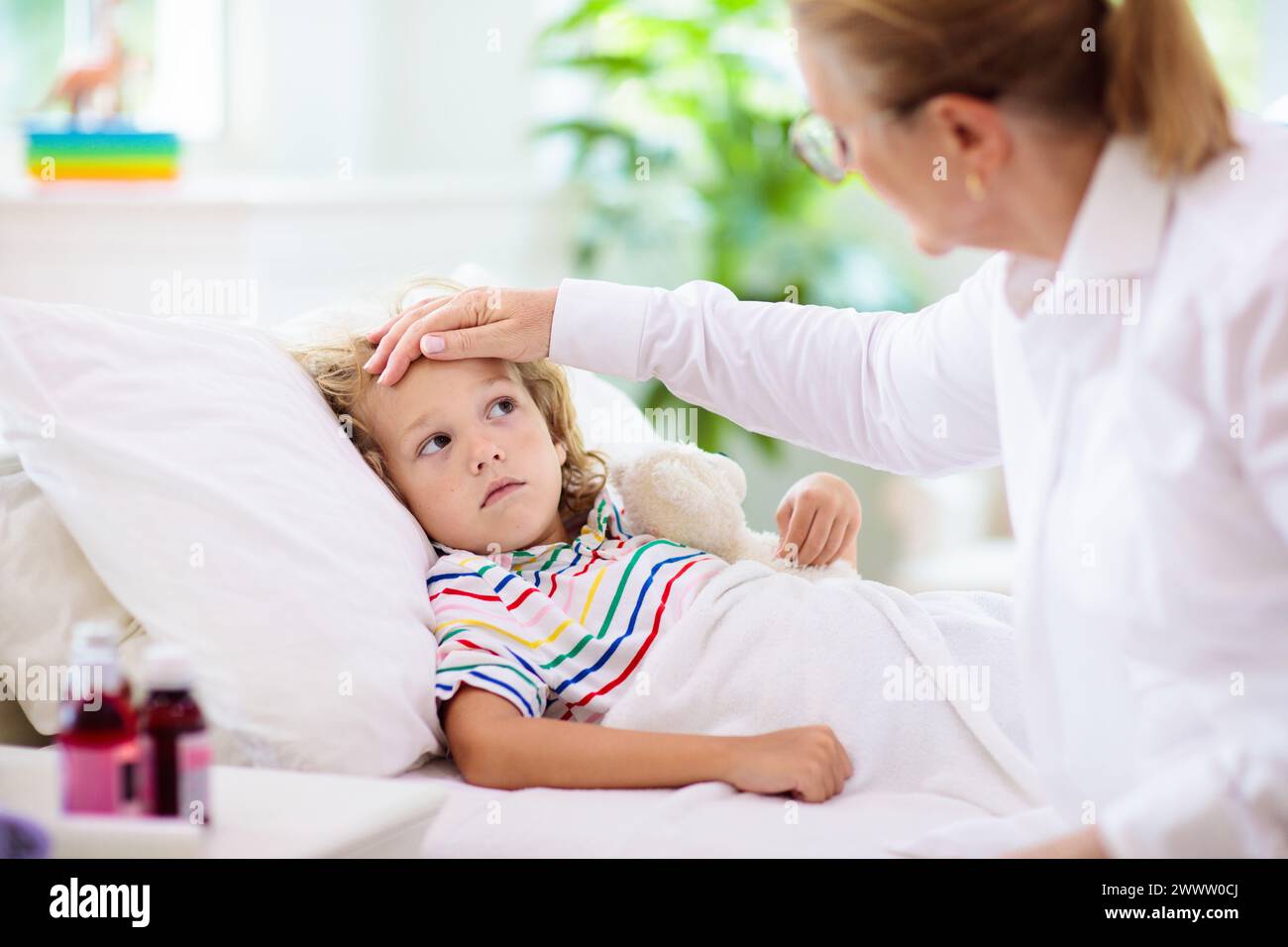 Sick little boy with medicine. Mother checking fever of ill child in bed. Unwell kid with ...