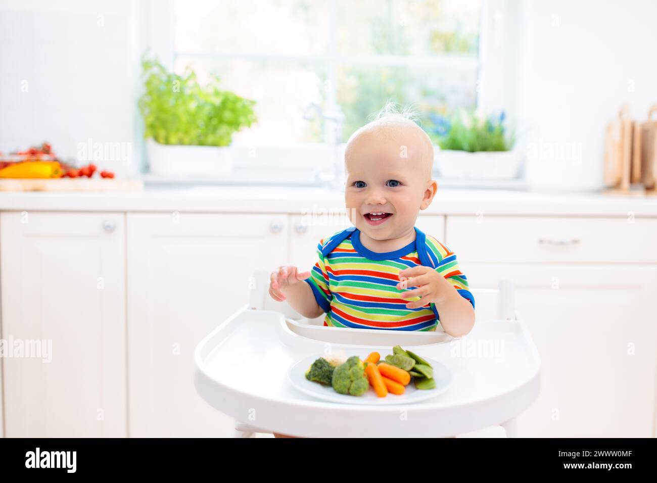 Cute baby eating vegetables in white kitchen. Infant weaning. Little ...