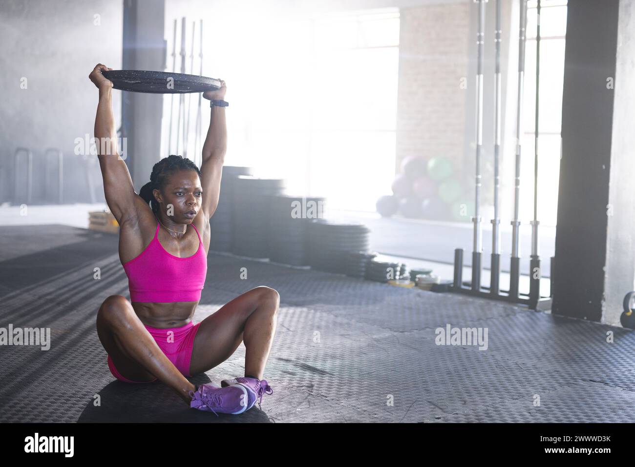 A fit African American strong woman lifts a weight plate overhead in ...