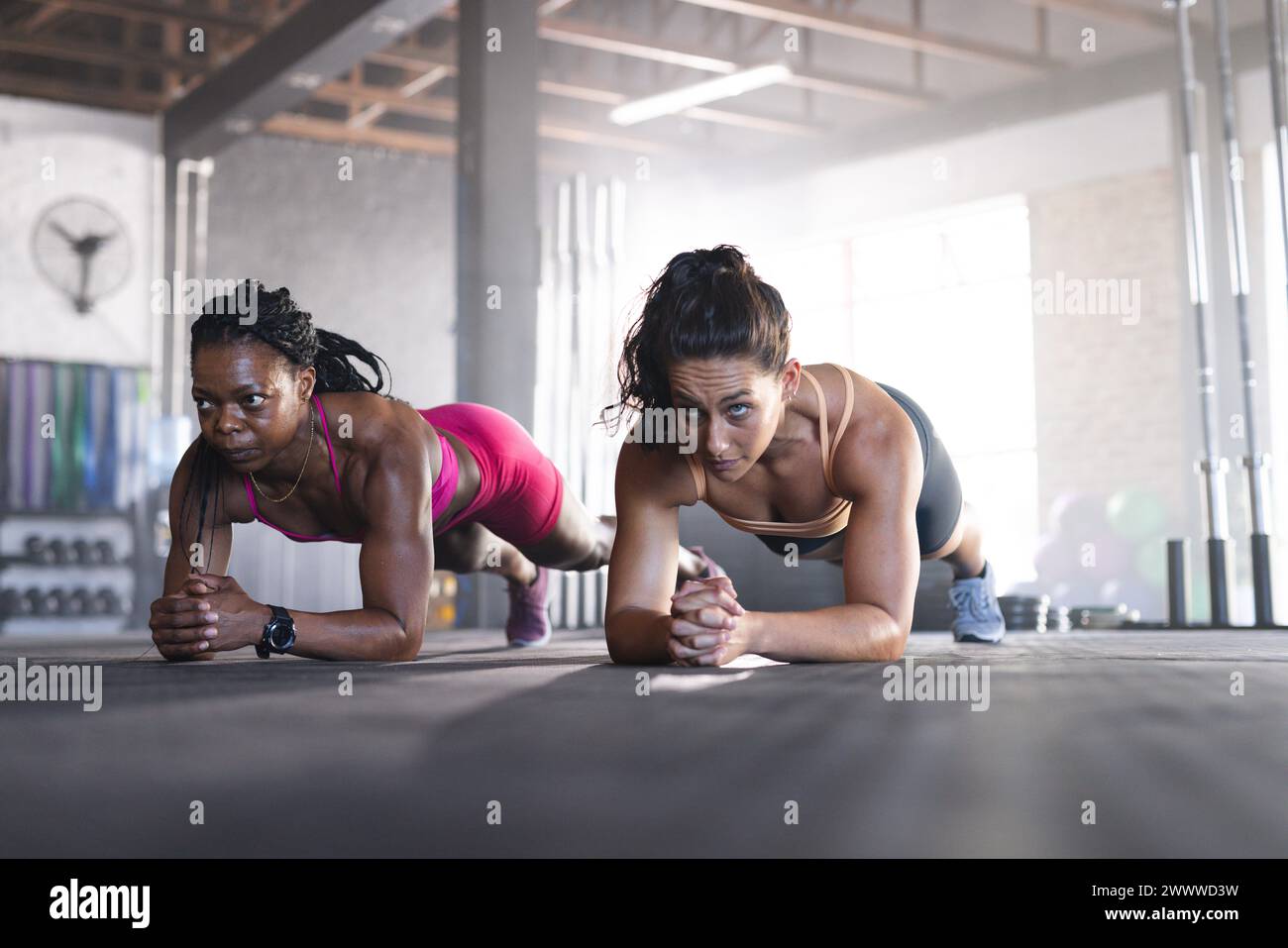 African American gym trainer and Caucasian trainee hold a plank ...