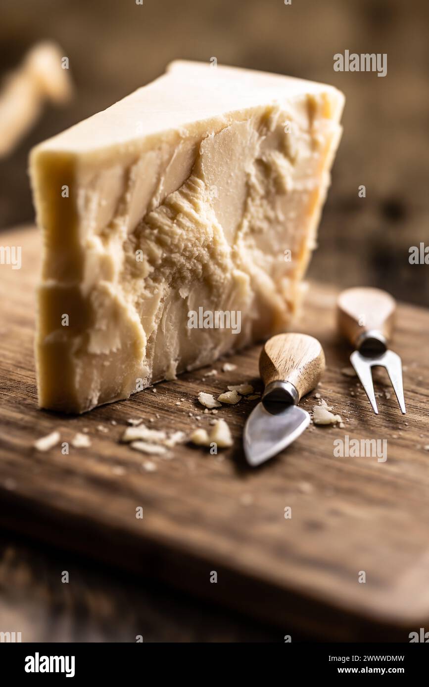 A block and pieces of Parmesan cheese on a cutting board along with a ...