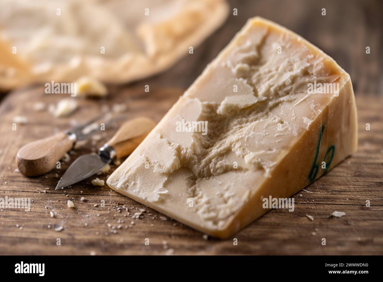 A block and pieces of Parmesan cheese on a cutting board along with a ...