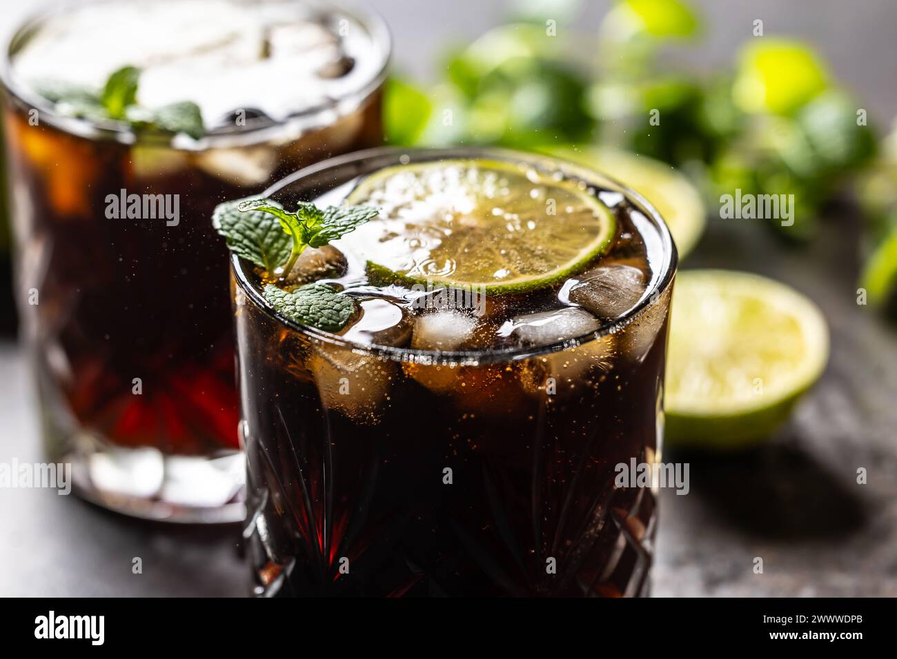 Tropical alcoholic cocktail Cuba Libre composed of white rum, cola, ice cubes, lime and mint ...