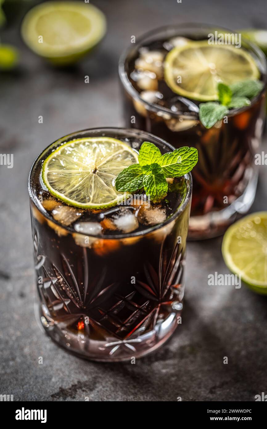 Tropical alcoholic cocktail Cuba Libre composed of white rum, cola, ice cubes, lime and mint ...
