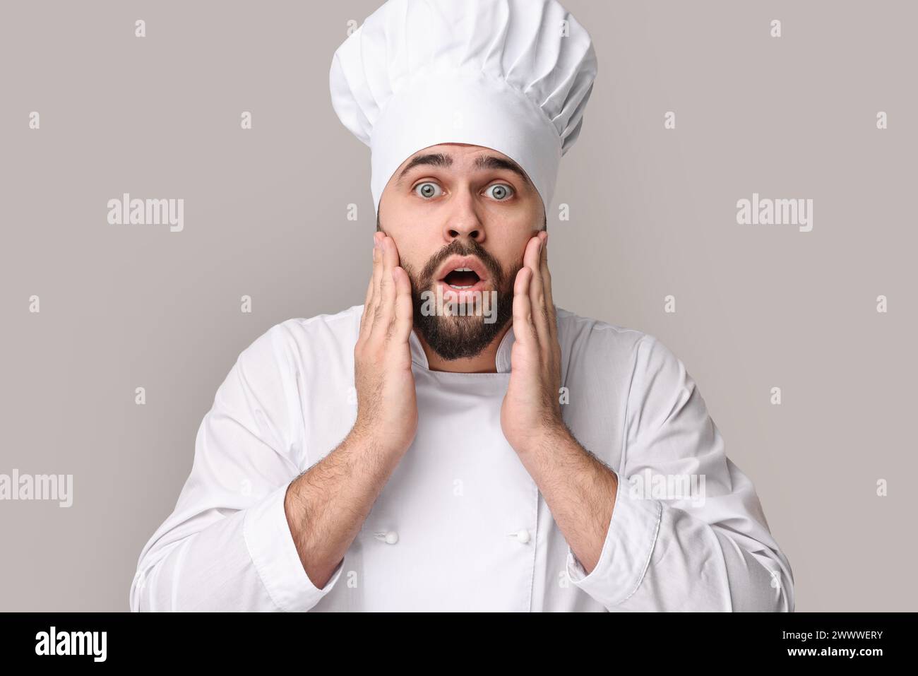 Surprised young chef in uniform on grey background Stock Photo - Alamy