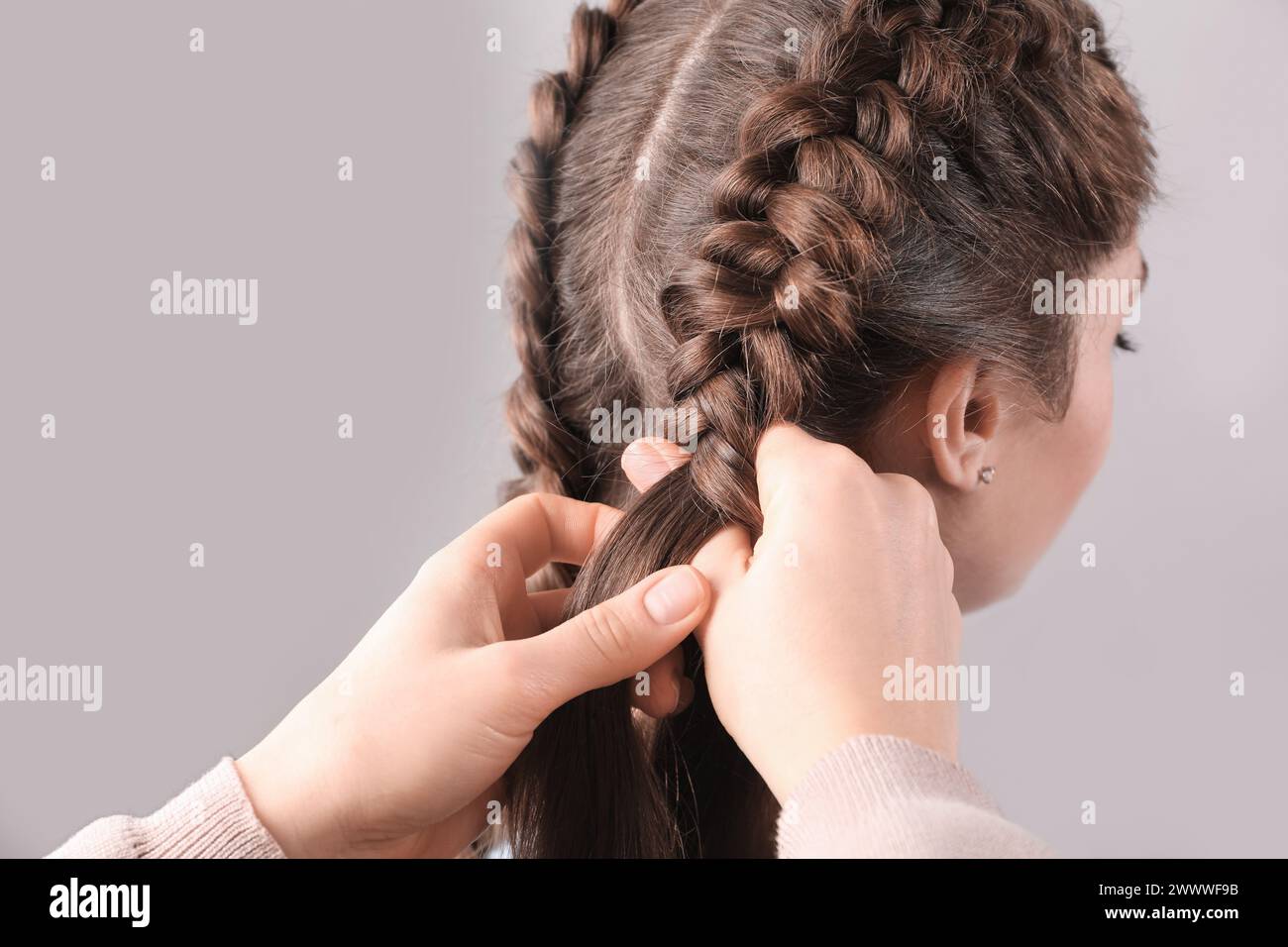 Professional stylist braiding woman's hair on grey background, closeup ...