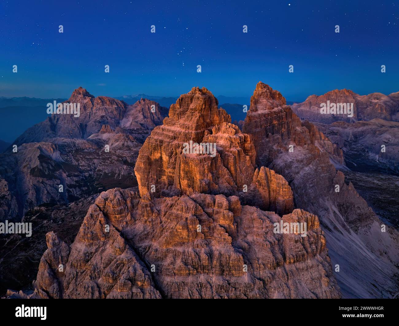 Aerial view from high altitude of Tre Cime di Lavaredo peaks orange lit ...