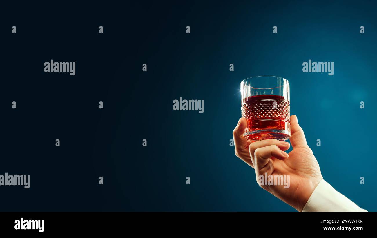 Male hand holds glass of whiskey, rum against gradient blue background ...