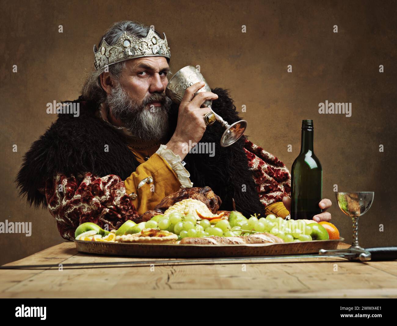 King, confident and feast at table with wine glass as royalty in studio ...