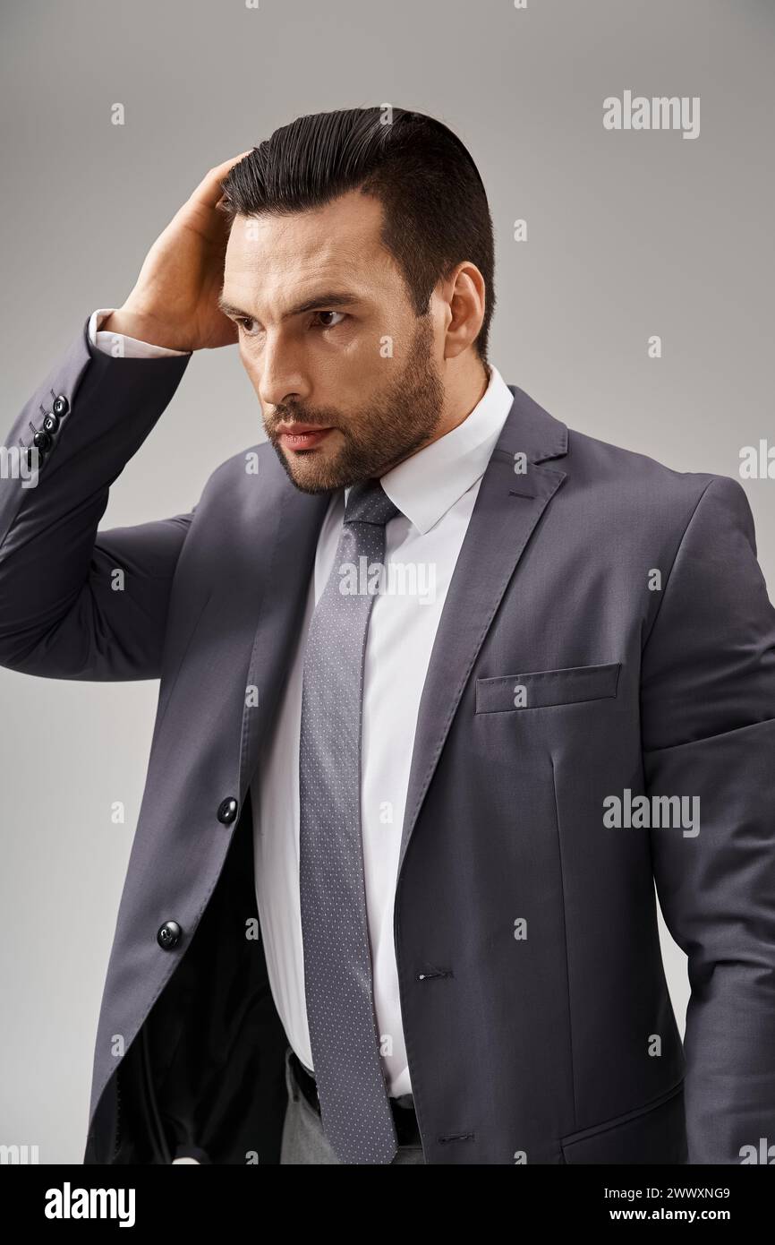 good looking man in formal wear with tie adjusting his hair on grey ...