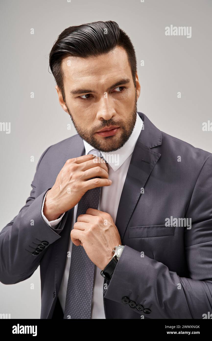 good looking man in formal wear adjusting his tie on grey background ...