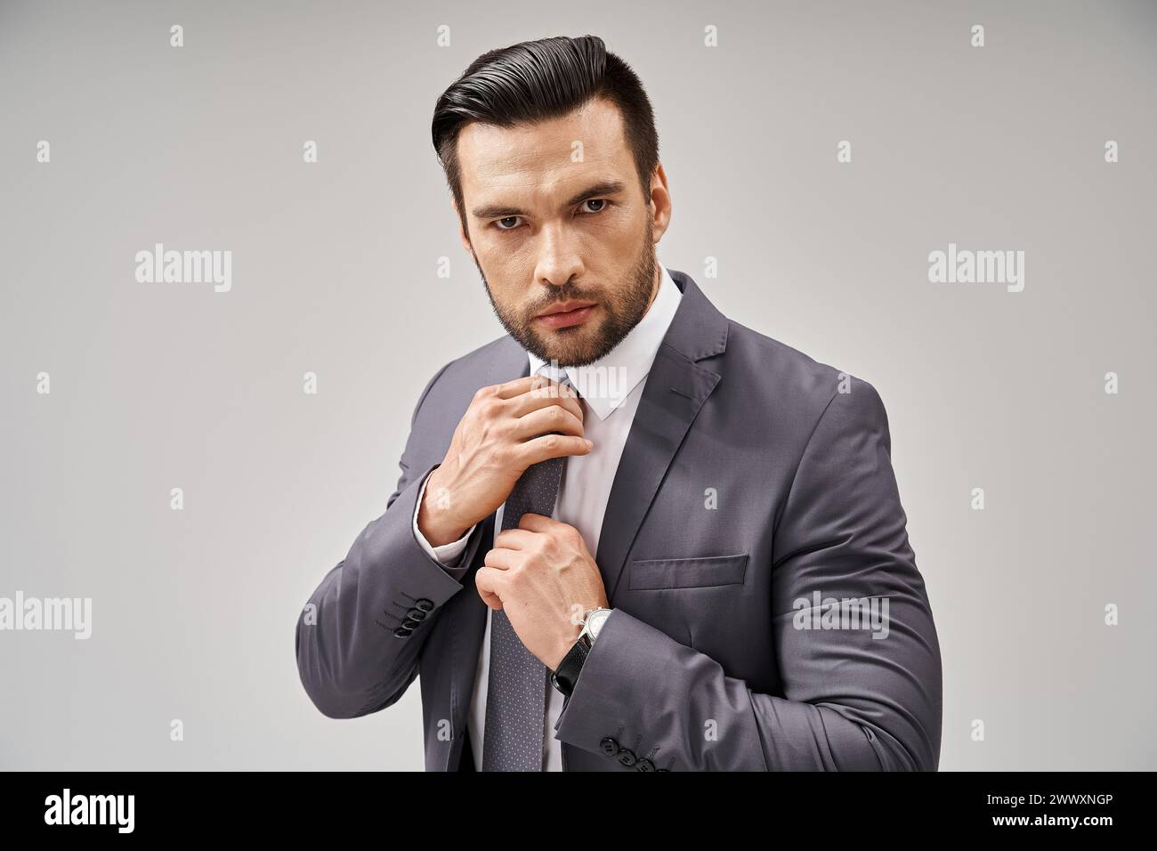 thoughtful man in formal wear adjusting his tie on grey background ...
