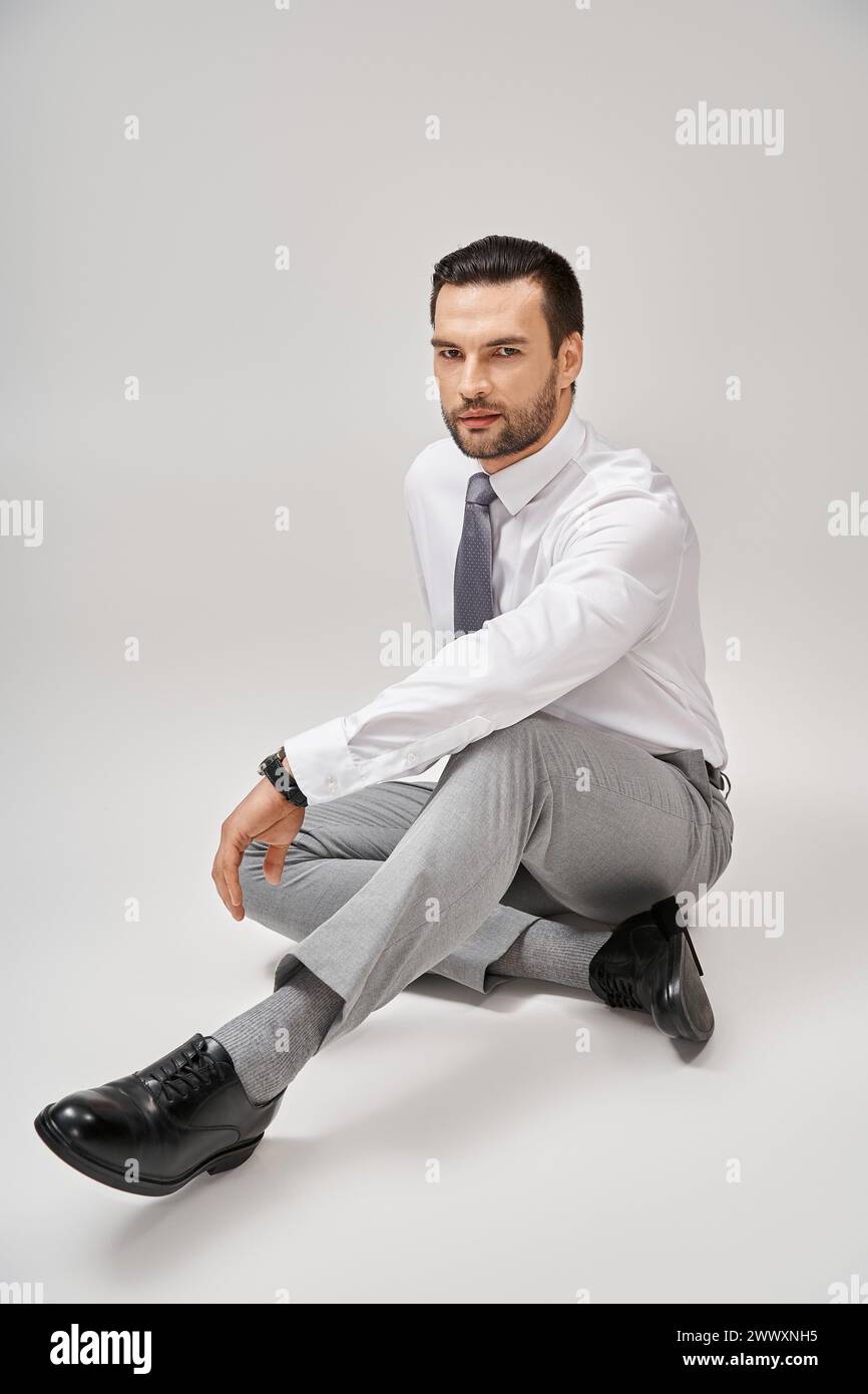 handsome businessman in elegant formal wear sitting on floor in studio ...