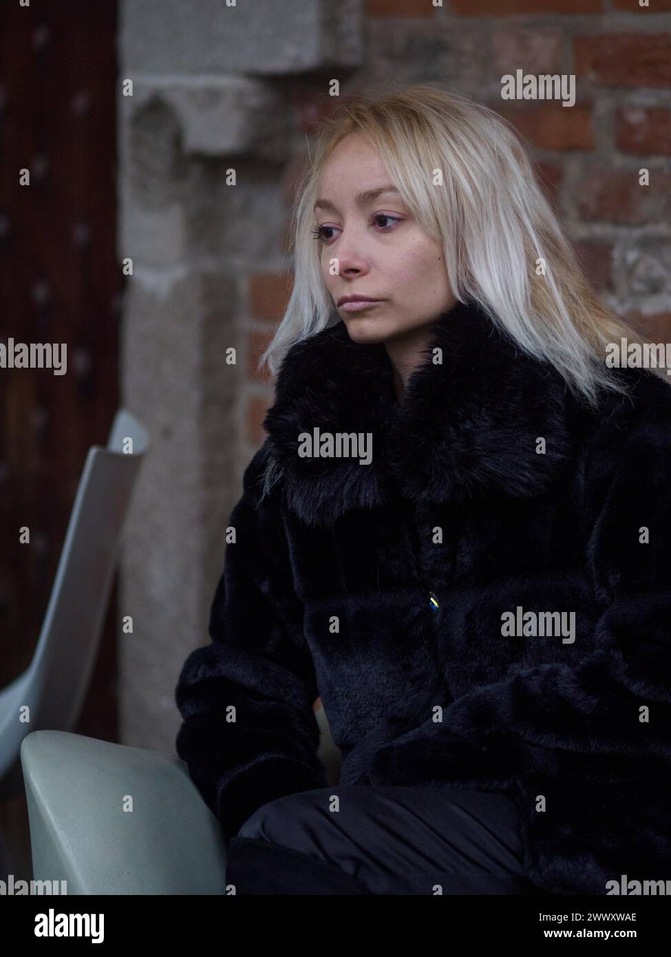 A pensive woman in fur coat sitting outside historic building in winter ...