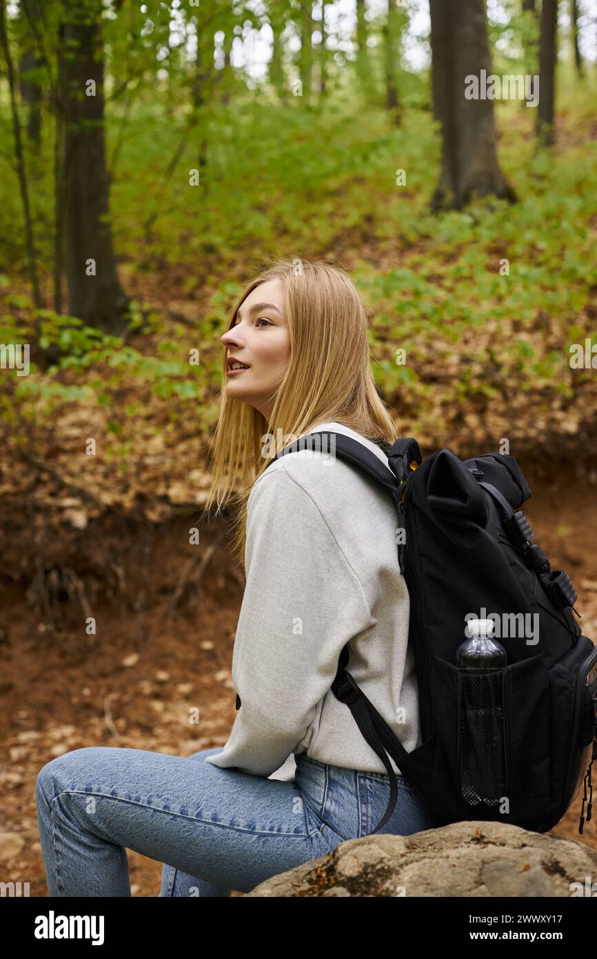 Side view of cozy smiling blonde woman hiker resting on rocks, looking ...