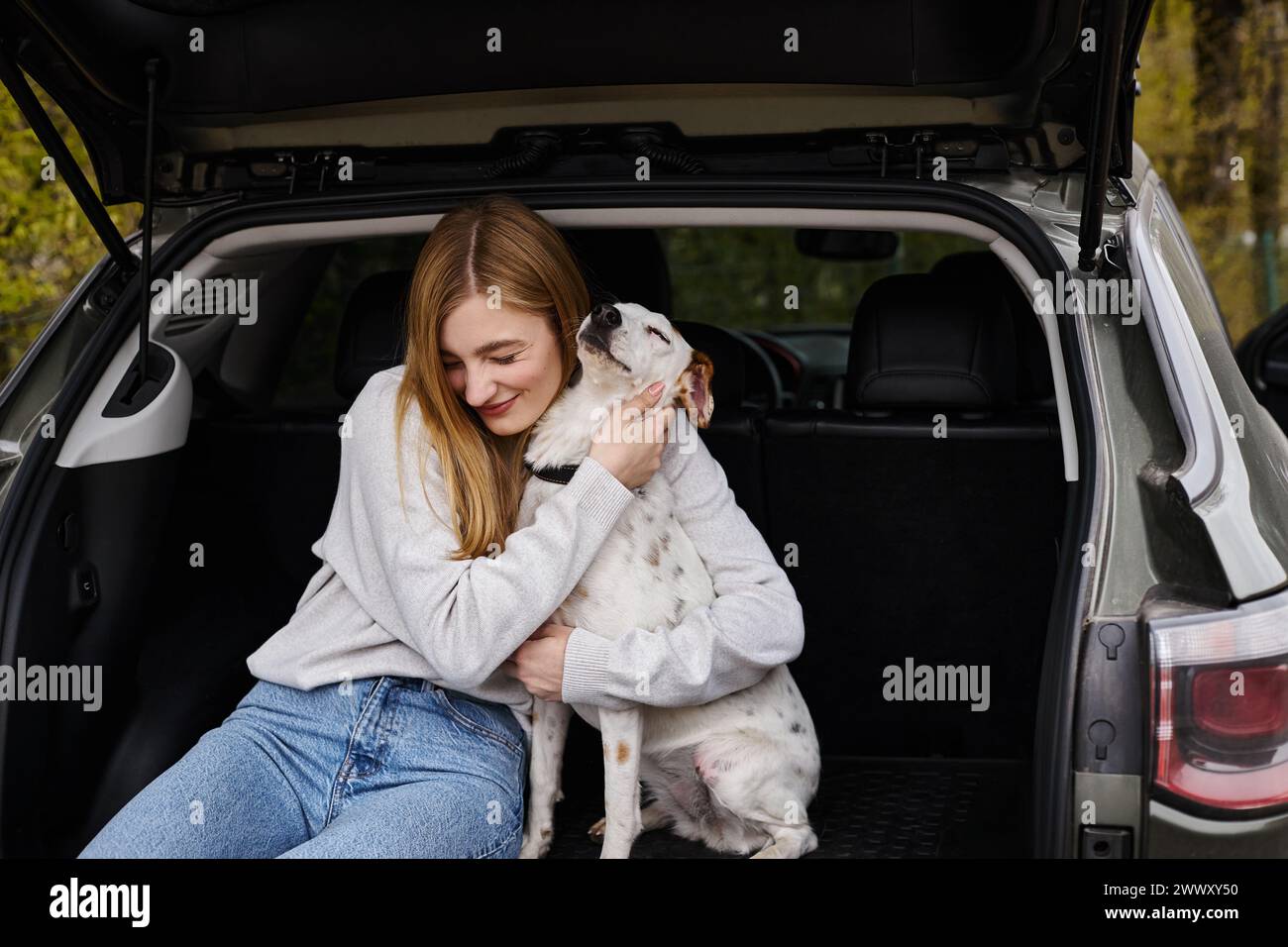 Image of woman gently hugging her white dog sitting at back of car. Dog ...