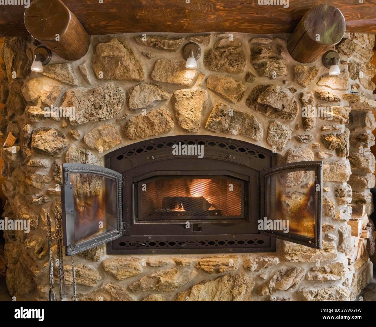 Lit fieldstone and porous rock fireplace in living room inside ...