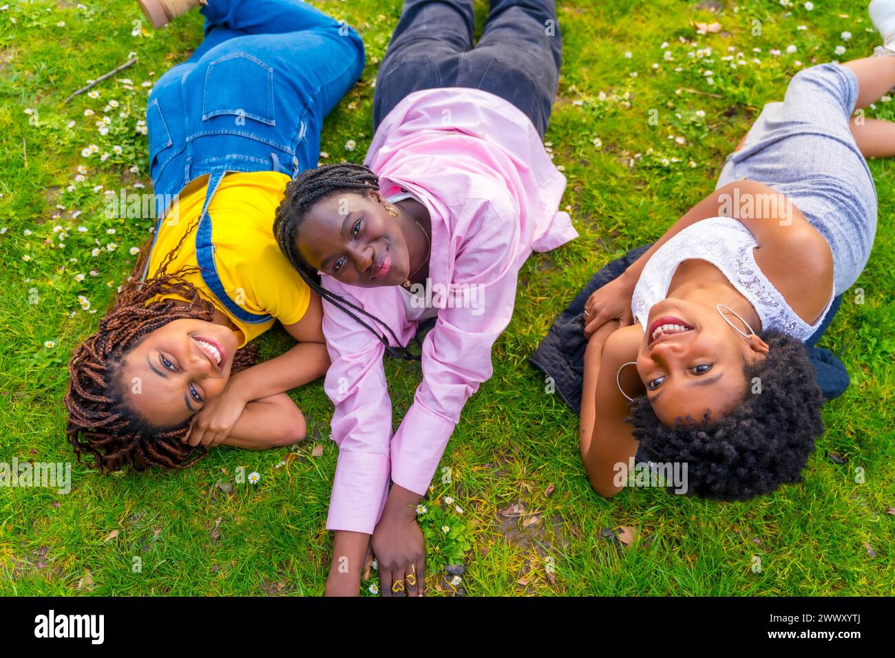 Three young female african friends enjoying spring lying on the green ...
