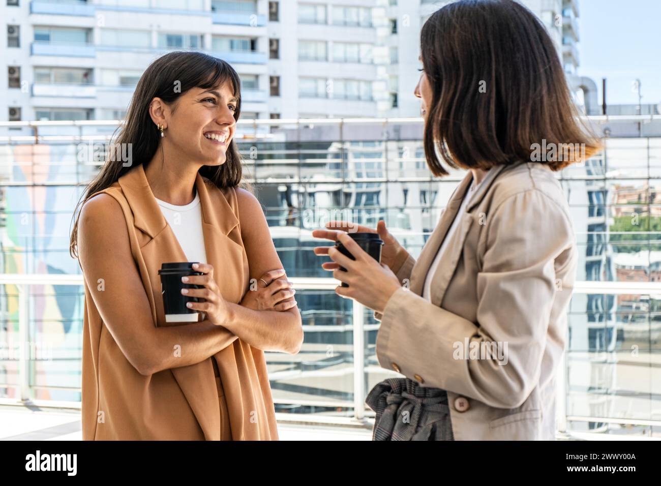 Two women are enjoying their coffee break outside, chatting and smiling ...