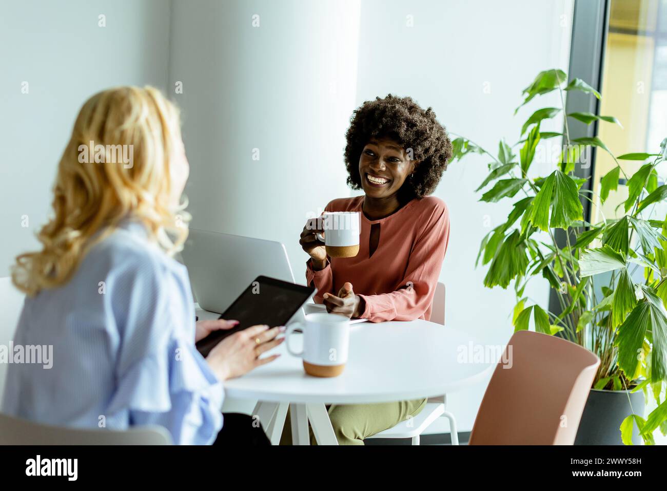 Two colleagues enjoying a cheerful conversation over coffee in a sunny ...