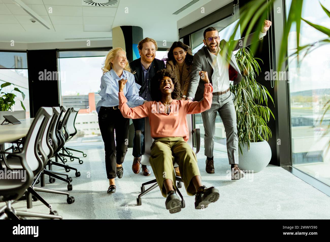 Team of coworkers shares a moment of fun, racing an office chair amidst ...