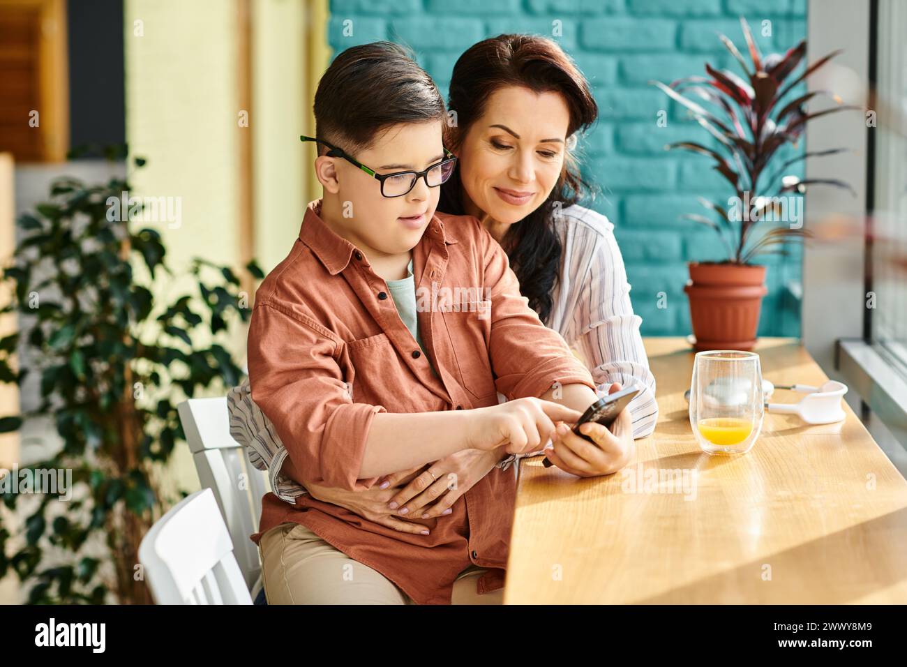 jolly mother spending quality time with her cheerful son with Down syndrome with smartphone ...