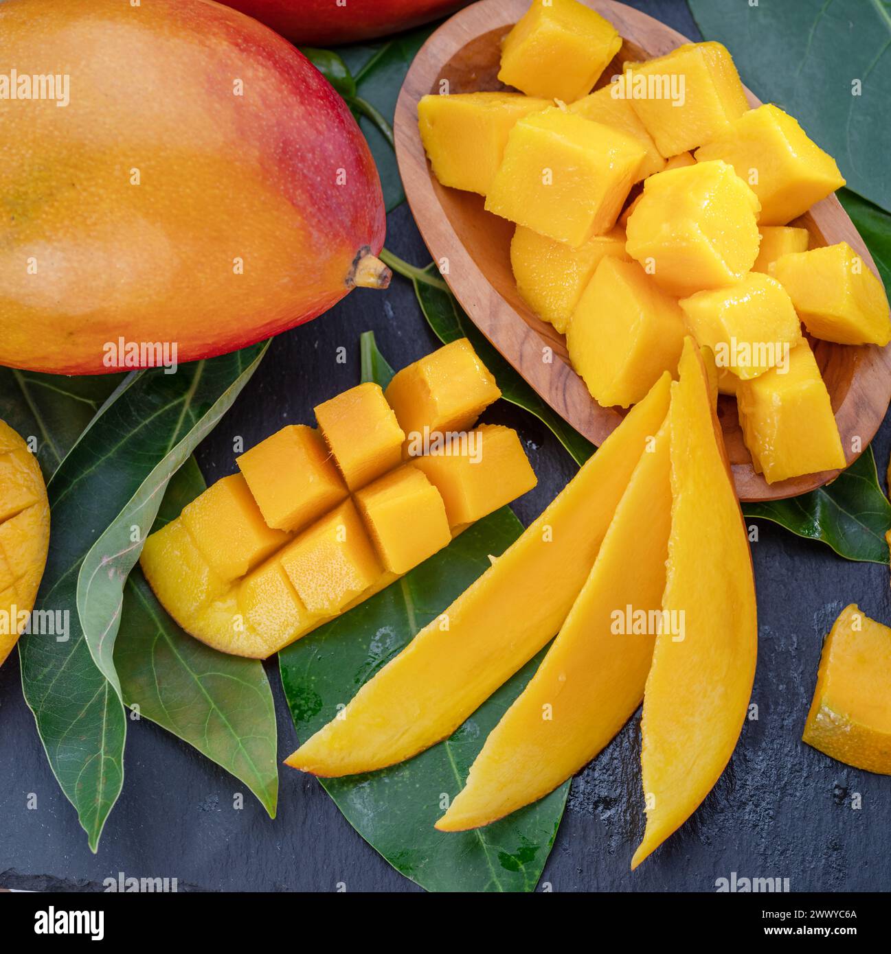 Ripe mango fruits with slices and mango leaves on a gray stone table ...