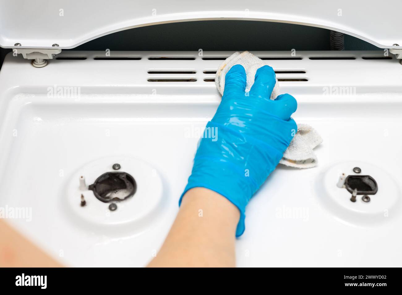 housewife in rubber gloves wipes gas stove. home gas stove care. a ...