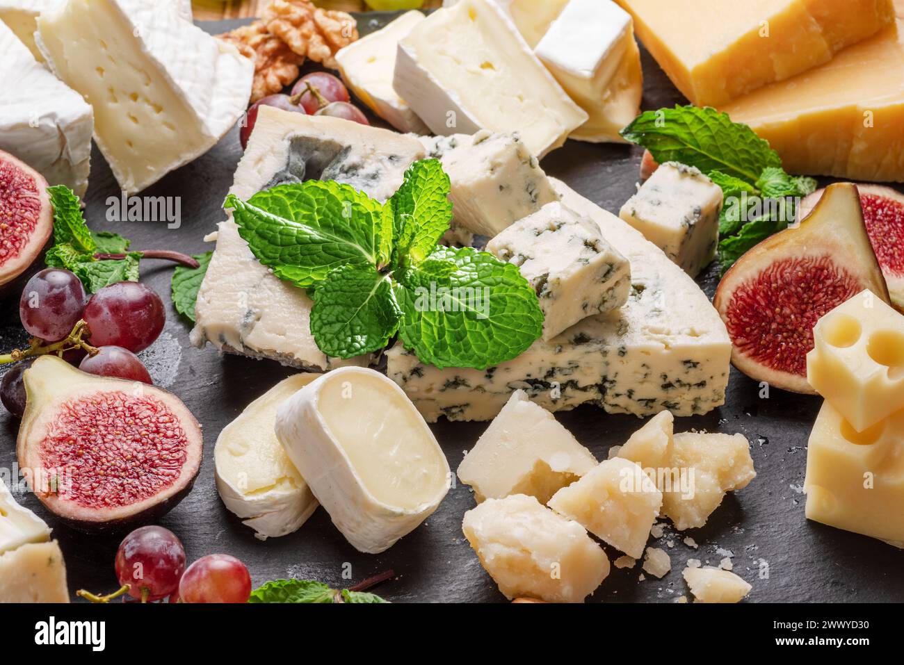 Variety of sliced cheeses with fruits, mint, nuts and cheese cutting ...