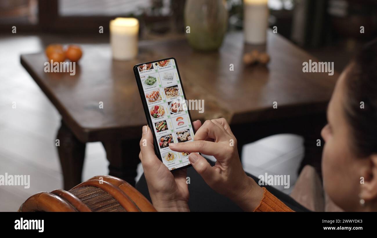 Ordering food using a smartphone at home. A woman selects sushi sets in ...
