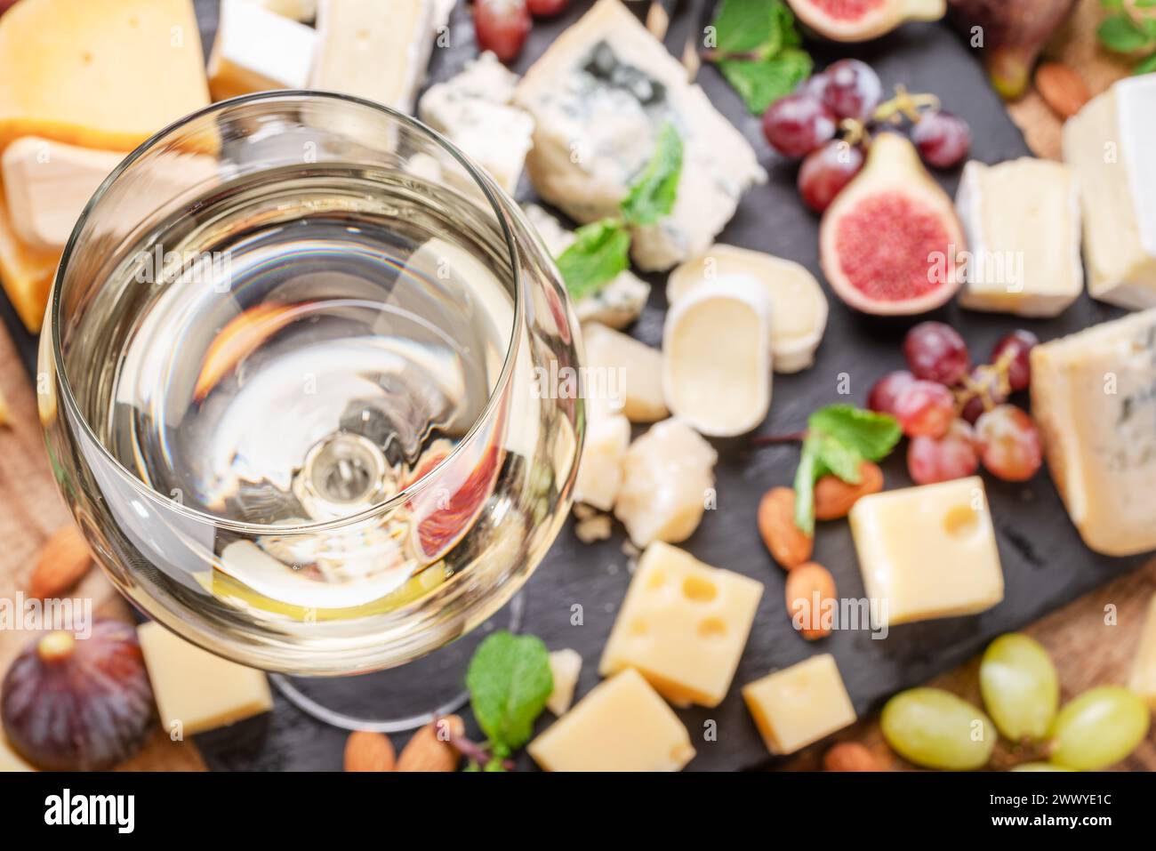 Glass of white wine with variety of sliced cheeses with fruits, mint ...