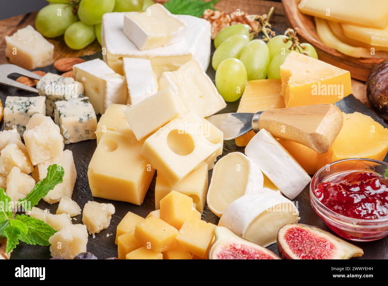 Variety of sliced cheeses with fruits, mint, nuts and cheese cutting ...