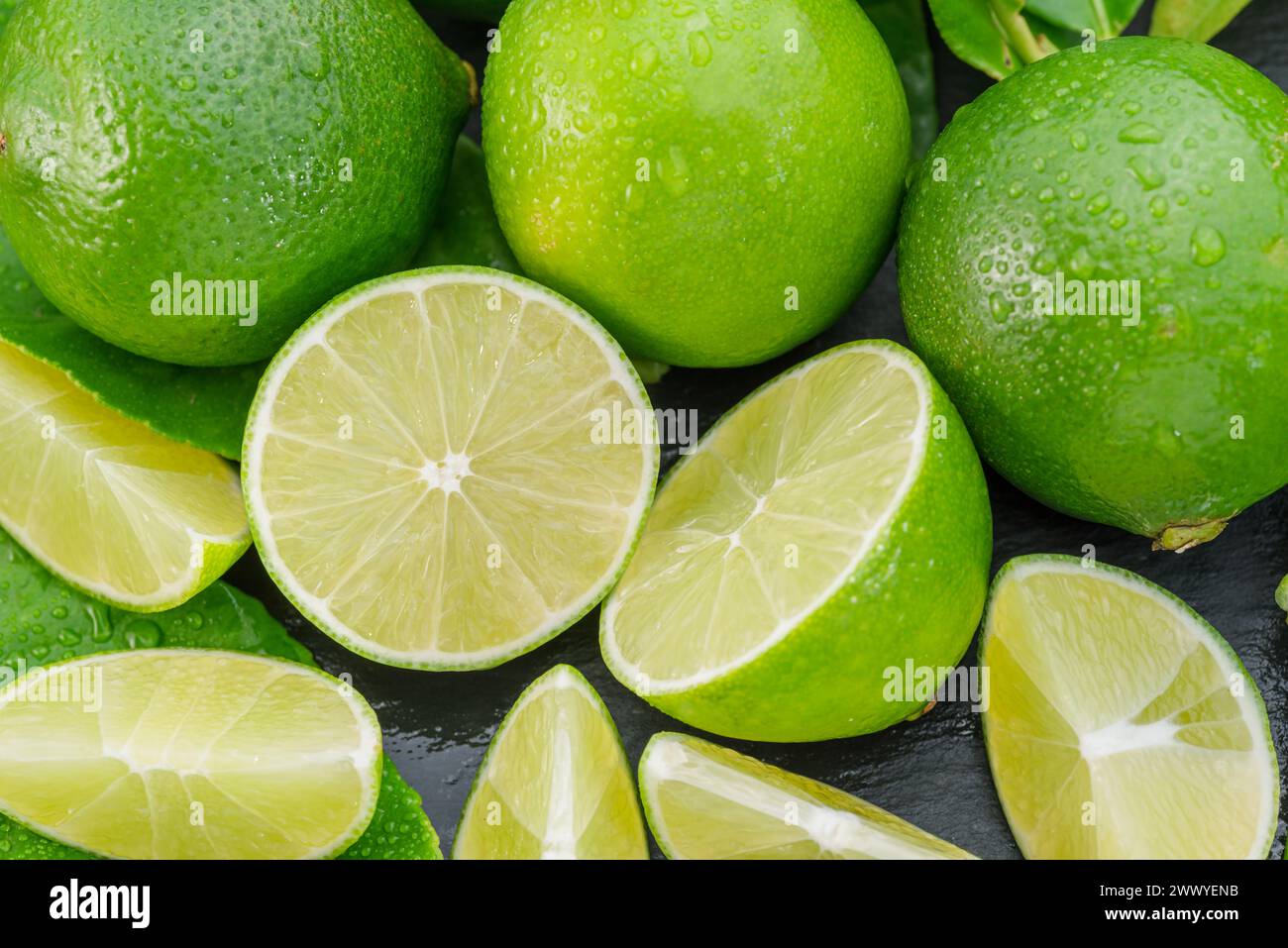 Ripe lime fruits with slices and lime leaves on a gray stone table ...
