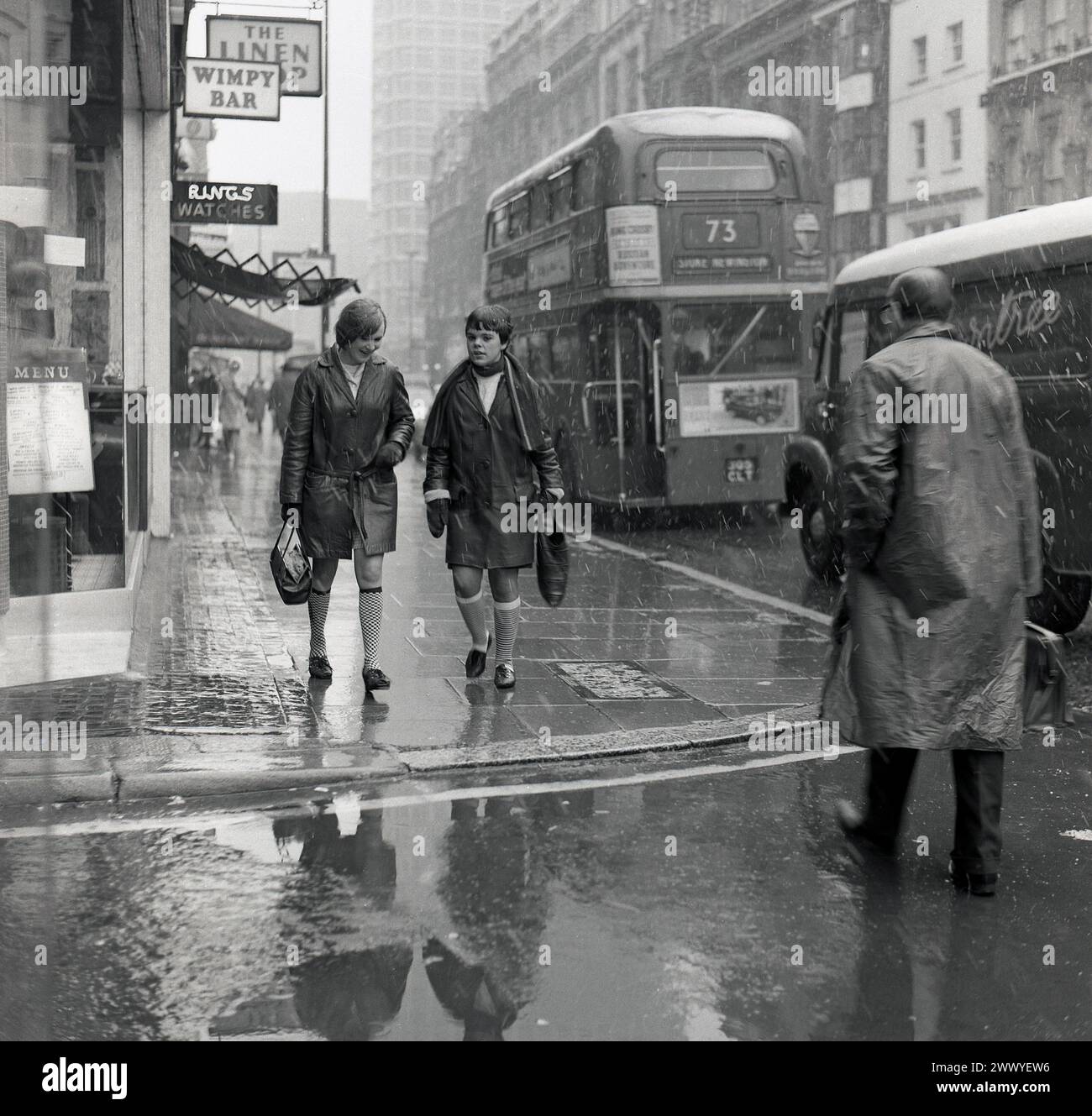 1960s, historical, two girls, wearing rainmacs, walking on the pavement ...