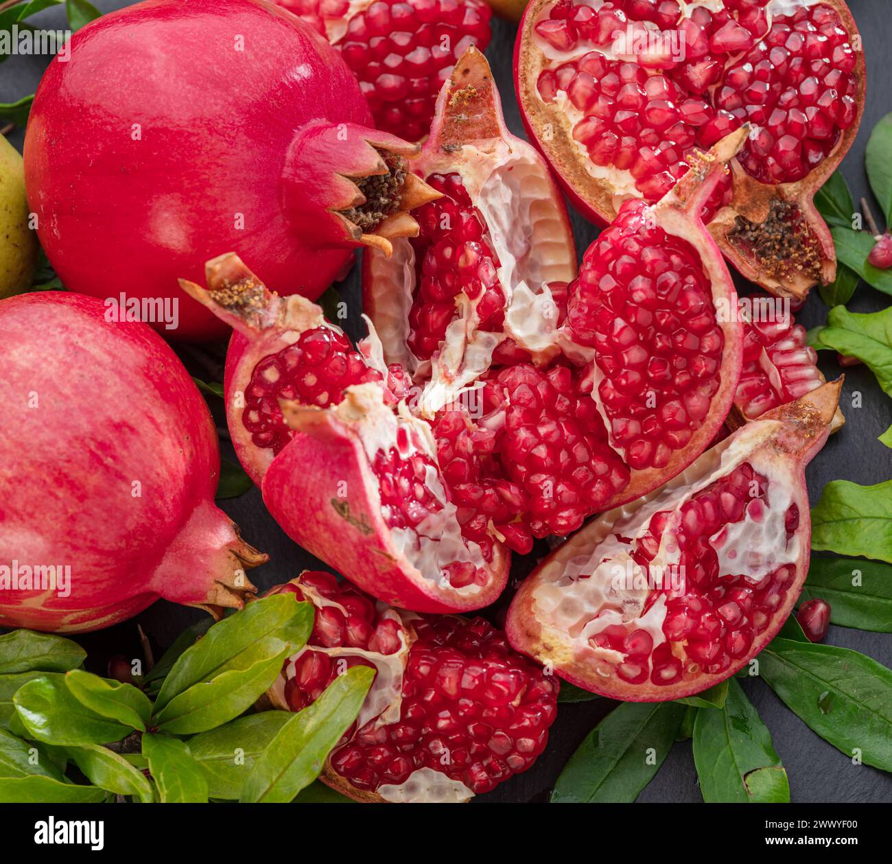 Ripe pomegranate fruits with slices and pomegranate tree leaves on a ...