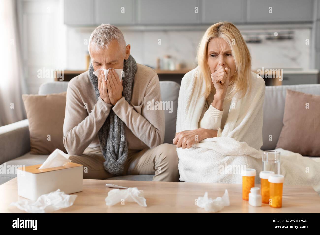 Sick couple blowing noses on couch Stock Photo - Alamy