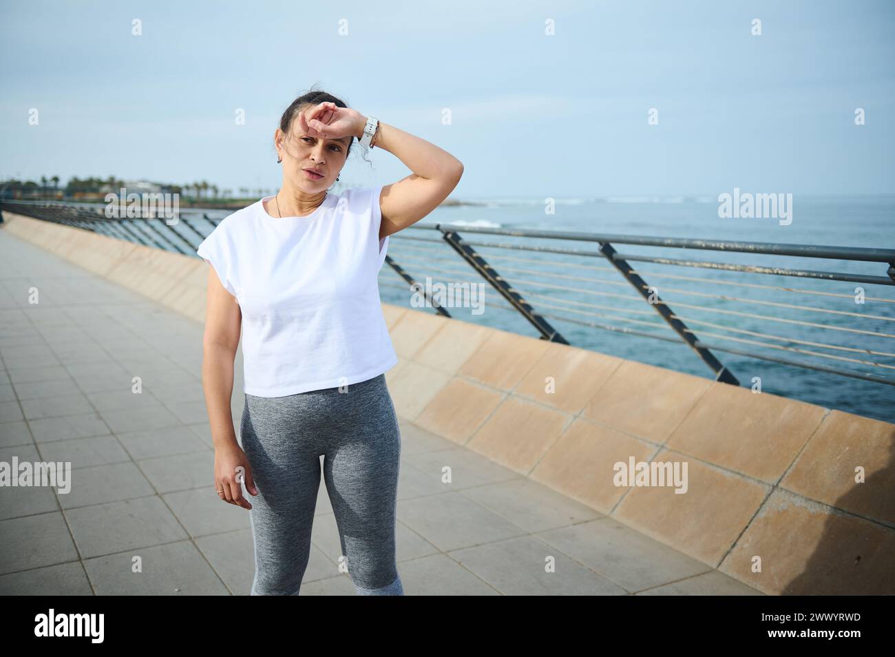 Exhausted young athlete in white t-shirt and gray leggings, a sporty ...