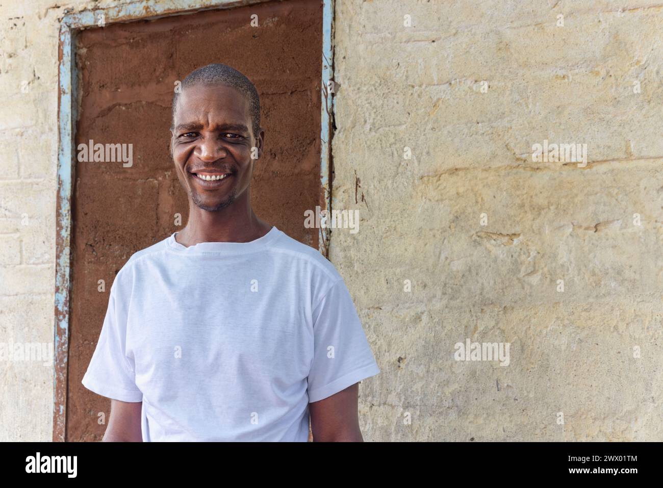 portrait of smiling african man standing next to a wall, village life ...