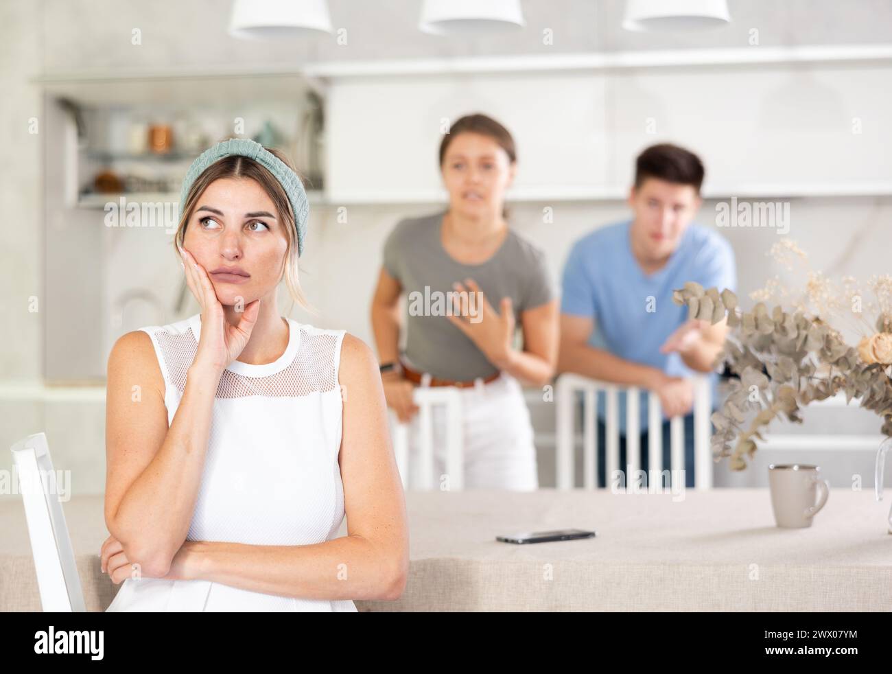 Disillusioned mother sitting in kitchen on background of dissatisfied ...