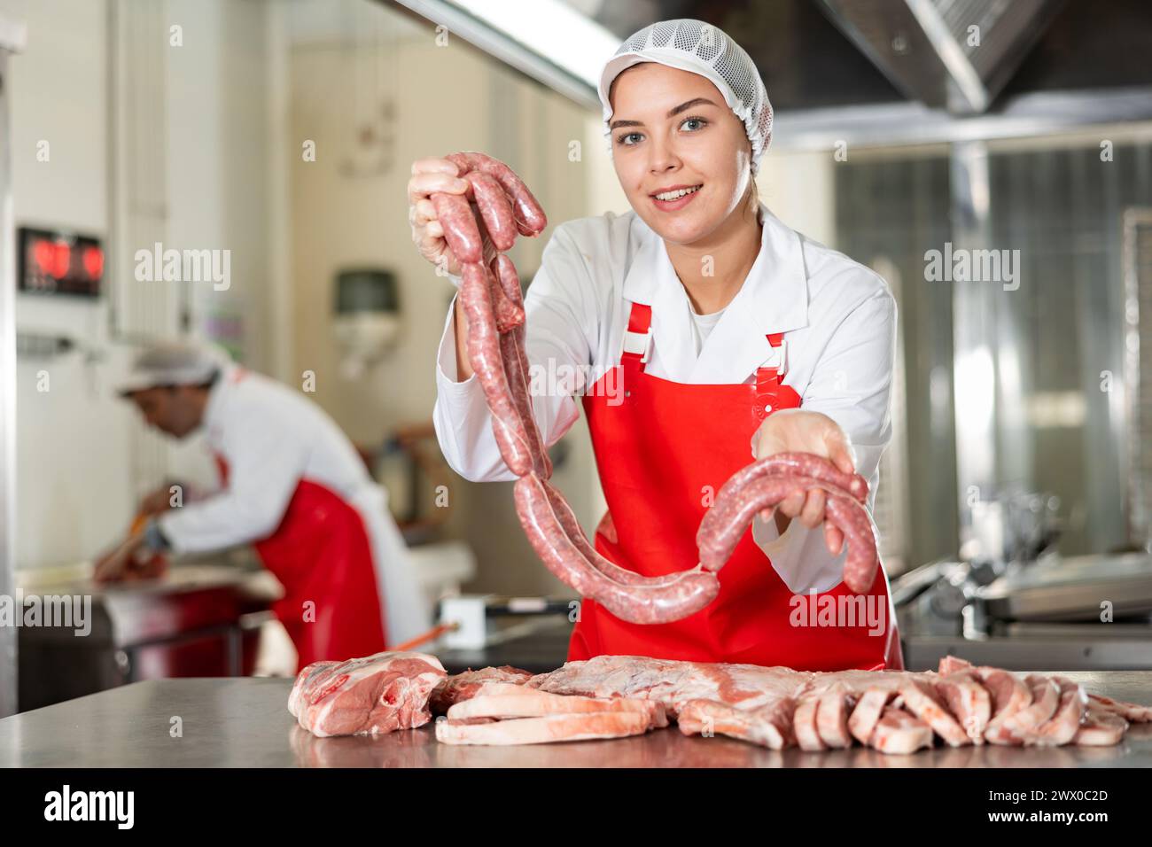 Female worker of meat processing factory demonstrating raw sausages ...