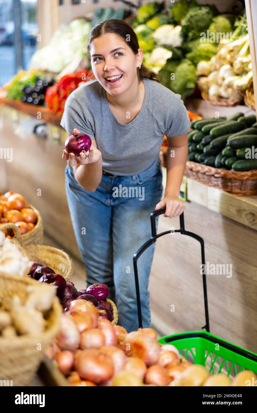 Woman picking out red onions to buy in fruit and vegetables aisle of ...